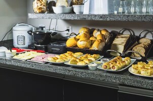 Disposição de buffet com diversos alimentos, incluindo pães, doces e fatias de carne.