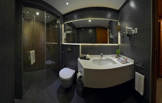 Casa de banho moderna com chuveiro envolto em vidro, sanita branca e toucador com espelho e porta-toalhas.