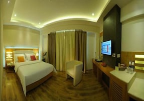 Quarto de hotel com cama, escrivaninha, cadeira, televisão e cortinas.