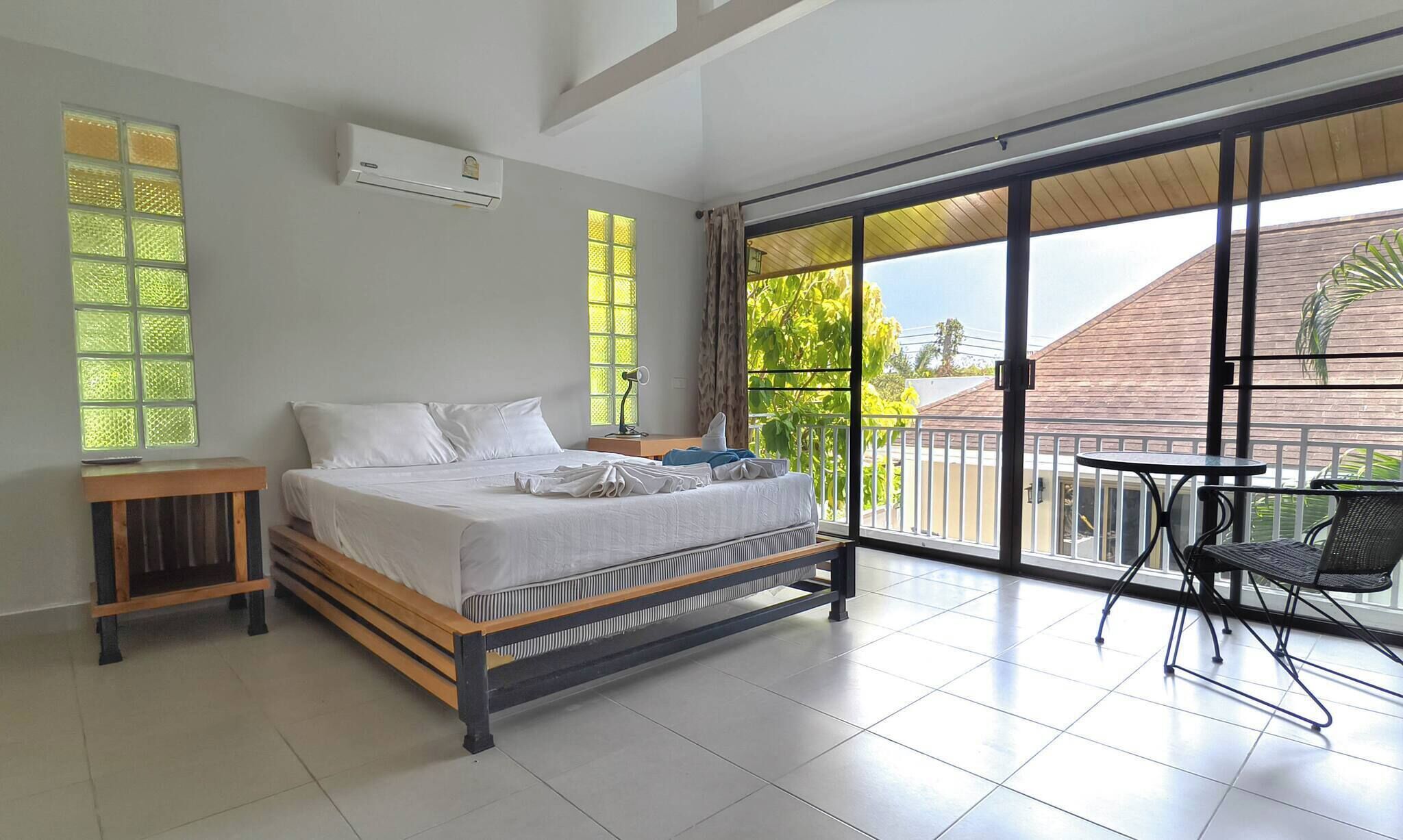 Quarto com cama, escrivaninha, cadeira e varanda com mesa.