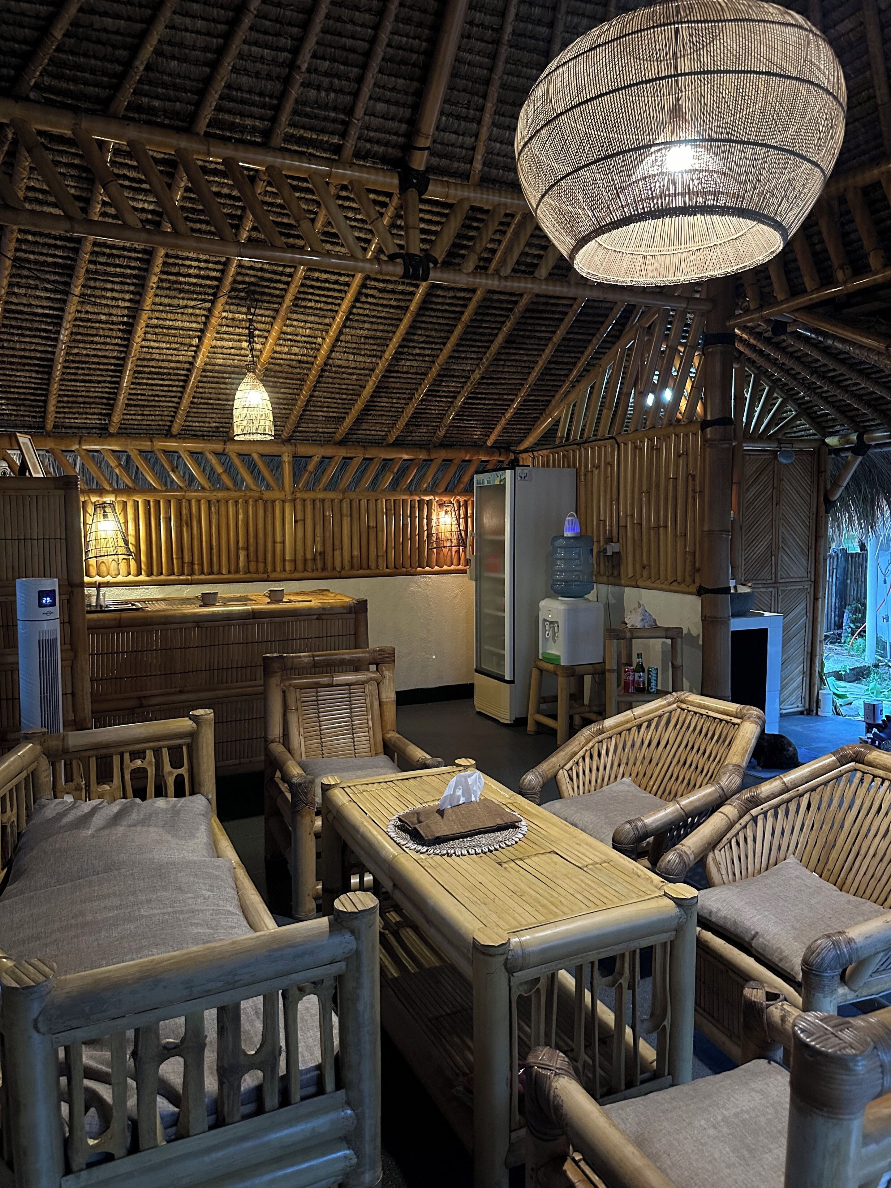 Quarto com móveis de bambu, luminária pendente e geladeira.