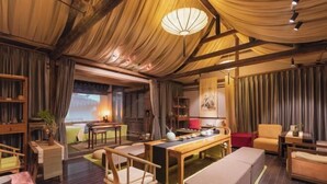Um quarto tipo tenda com uma mesa de madeira, cadeiras, um sofá e um lustre.