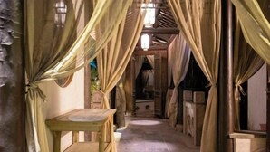 Um corredor estreito com cortinas penduradas, uma mesa de madeira e piso de pedra.