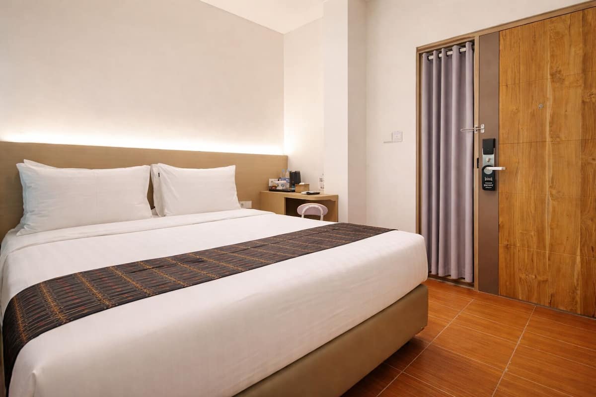 Quarto de hotel com cama, mesa de cabeceira, guarda-roupa de madeira e porta de banheiro.