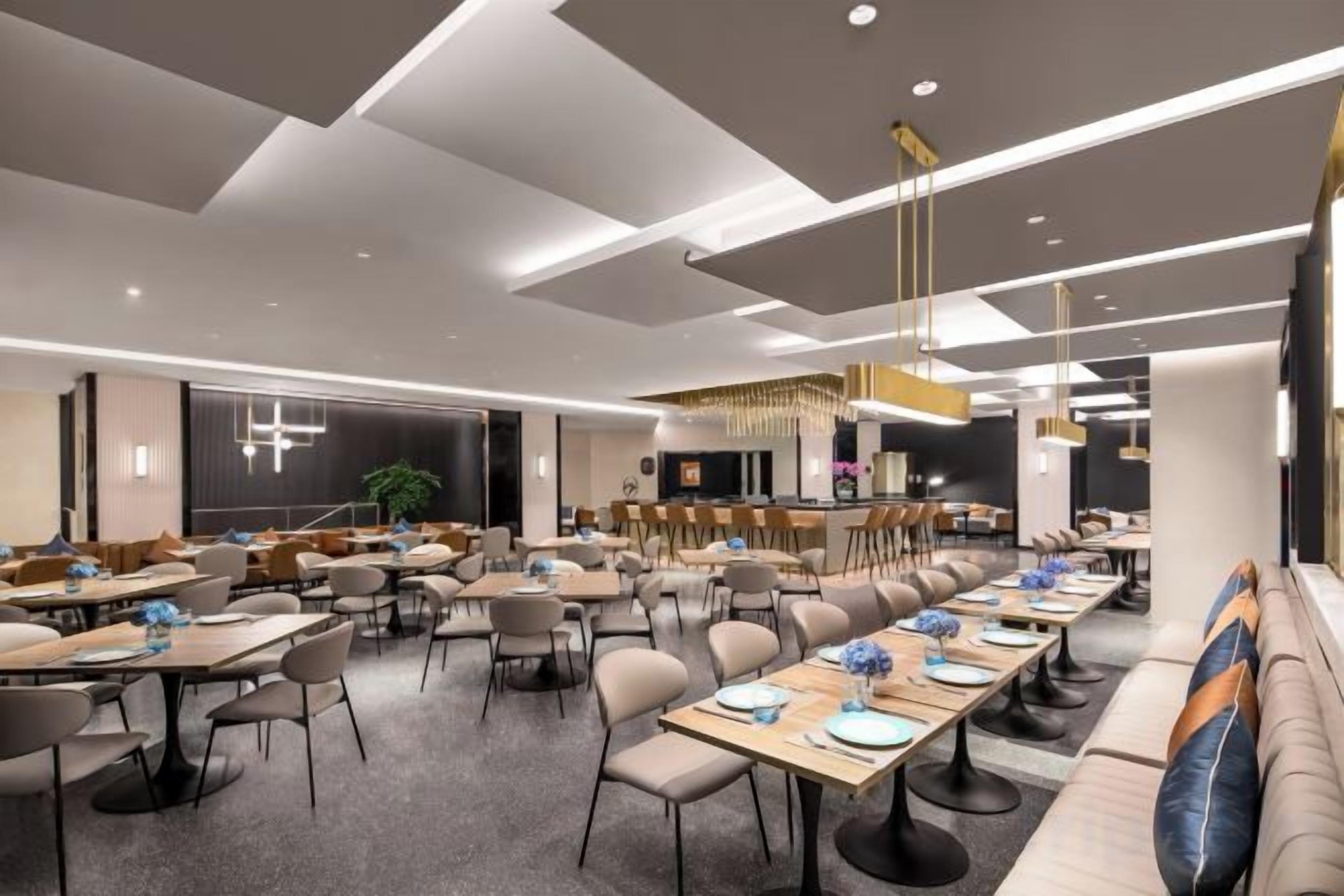 Uma sala de jantar moderna com várias mesas e cadeiras, um bar e luminárias contemporâneas.