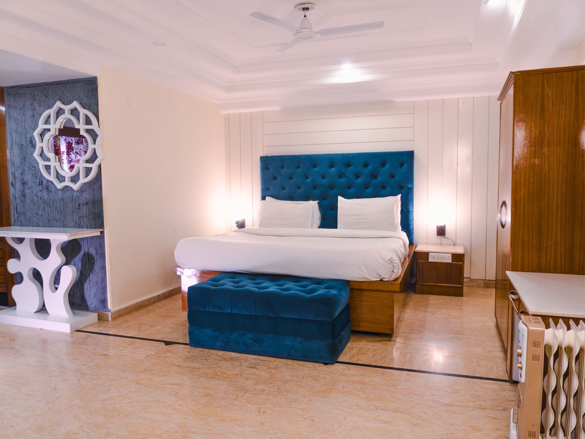 Quarto com uma cama grande, guarda-roupa de madeira, mesa de cabeceira branca e um objeto decorativo na parede.