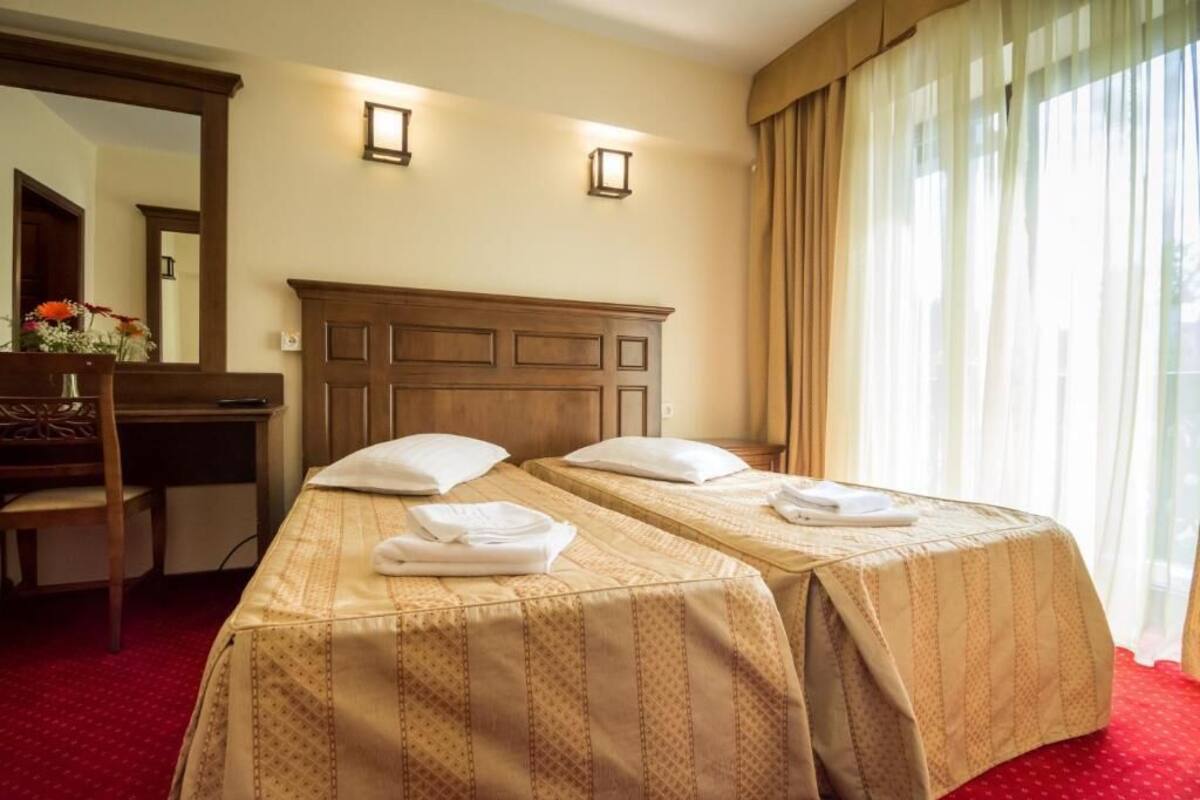 Quarto de hotel com duas camas, uma escrivaninha, uma cadeira e um espelho grande.