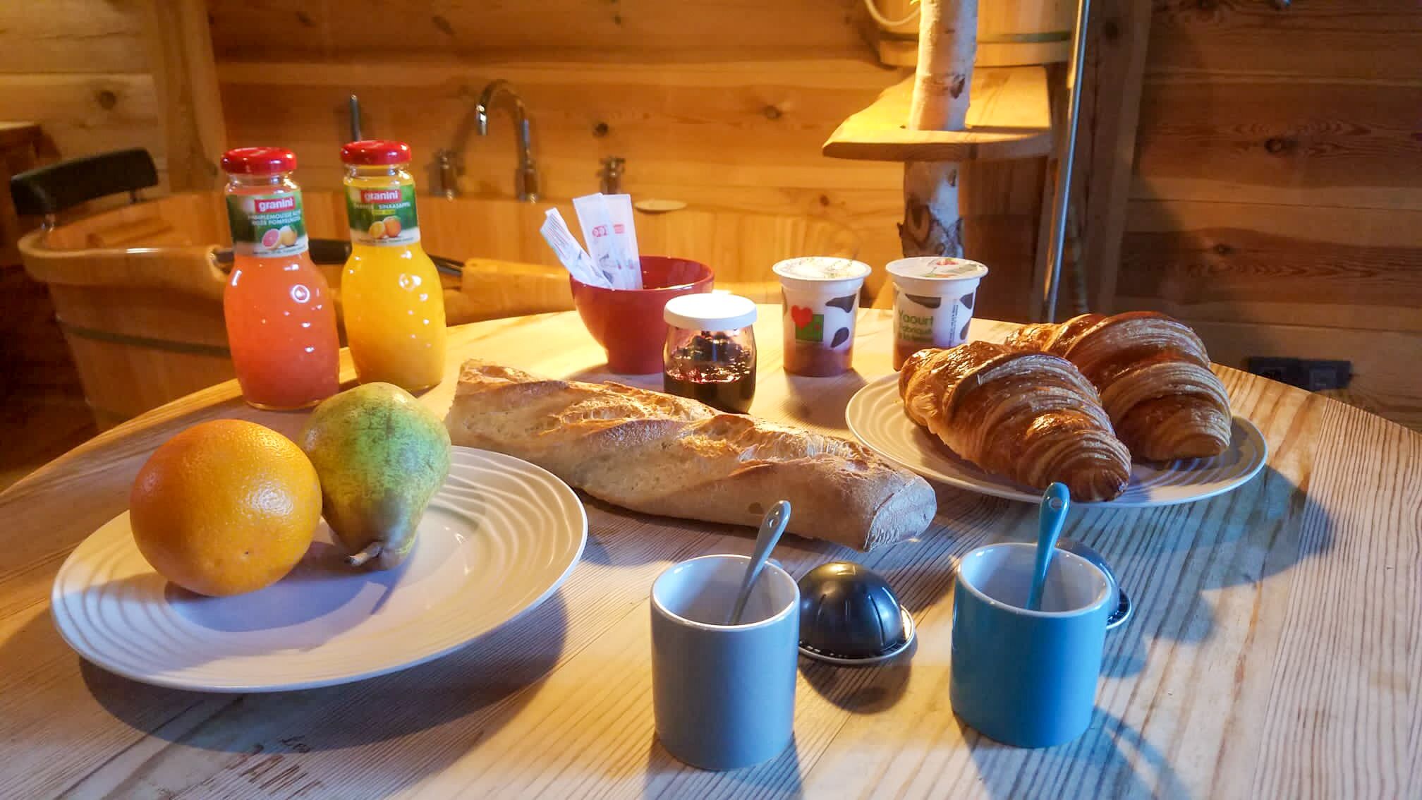 Uma mesa de café da manhã com croissants, frutas, suco e xícaras de café.
