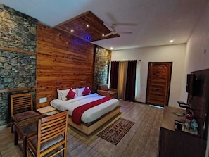 Quarto com cama, cabeceira de madeira, parede de pedra e ventoinha no teto.