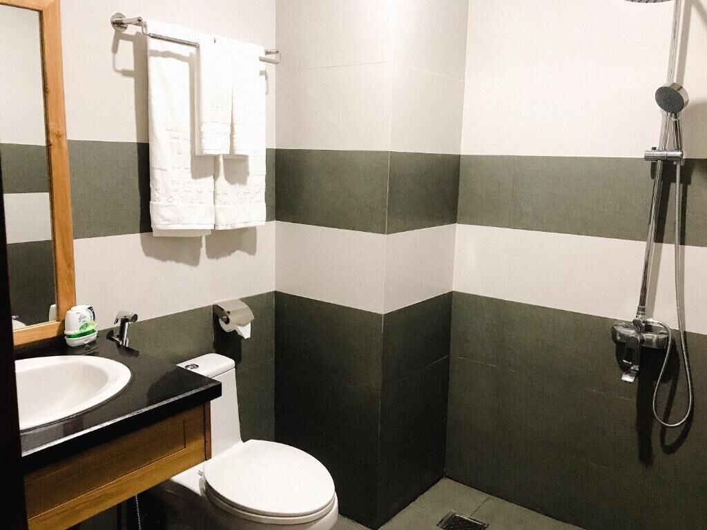 Casa de banho com lavatório, sanita, espelho, porta-toalhas e chuveiro.