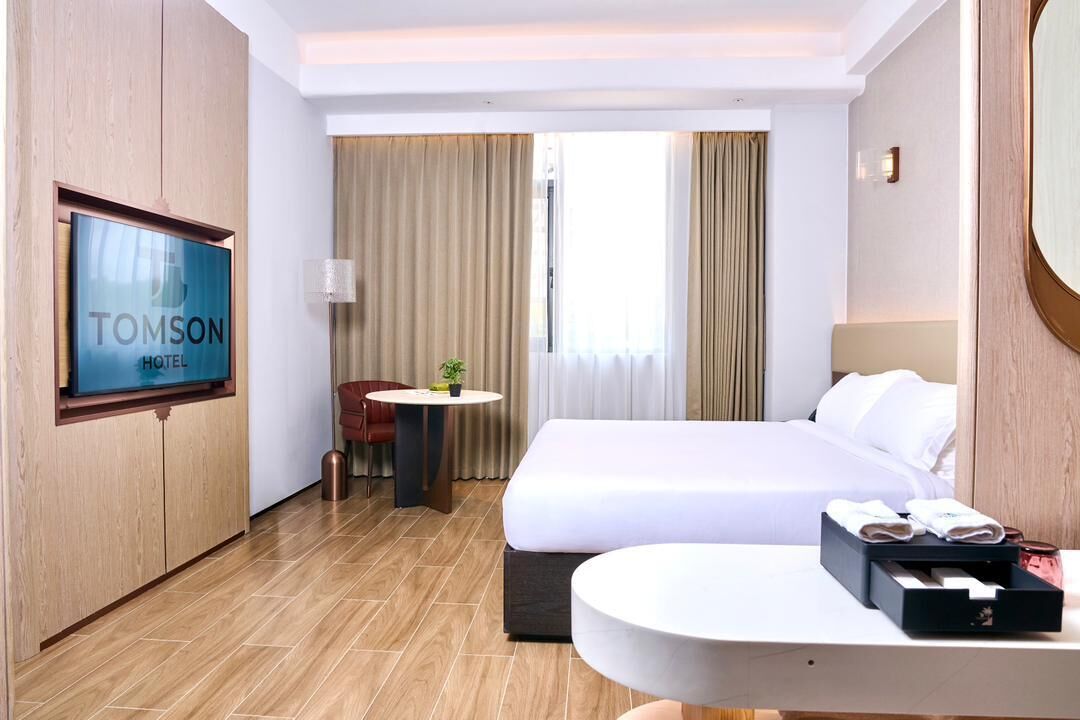 Quarto de hotel com cama, televisão, escrivaninha, cadeira e janela com cortinas.