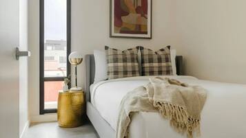 Quarto com cama, janela, obra de arte emoldurada e mesa de cabeceira com abajur.
