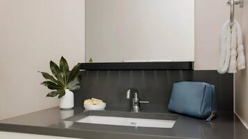 Uma casa de banho moderna com uma pia, uma planta em vaso, um porta-toalhas e uma bolsa azul.