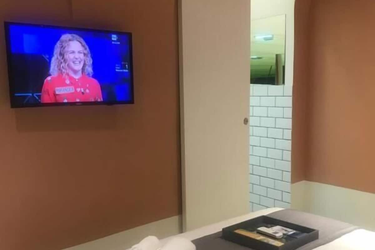 Quarto de hotel com uma cama, uma televisão na parede, uma porta e uma janela.