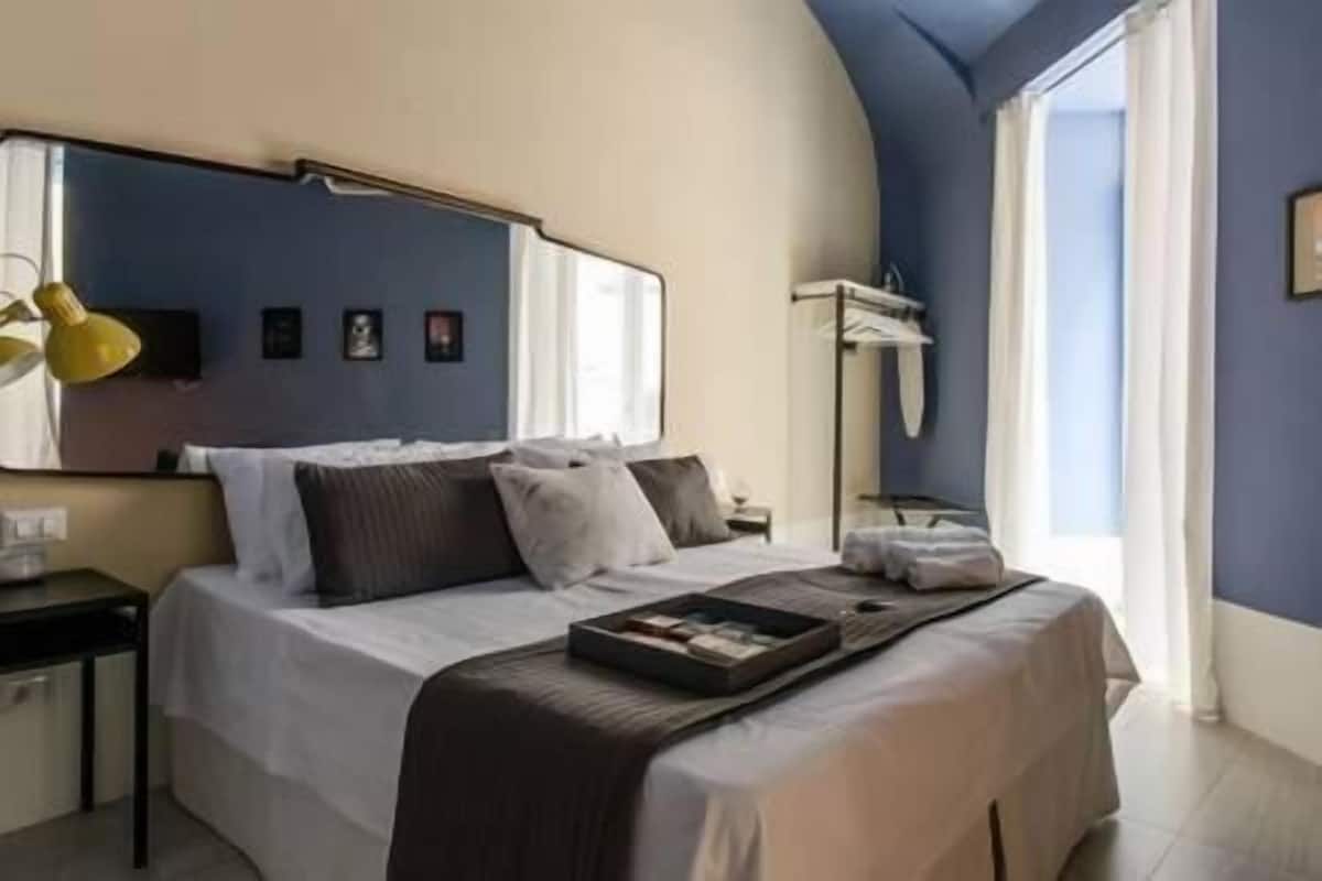 Quarto com cama, mesas de cabeceira, luminária, janela e espelho.