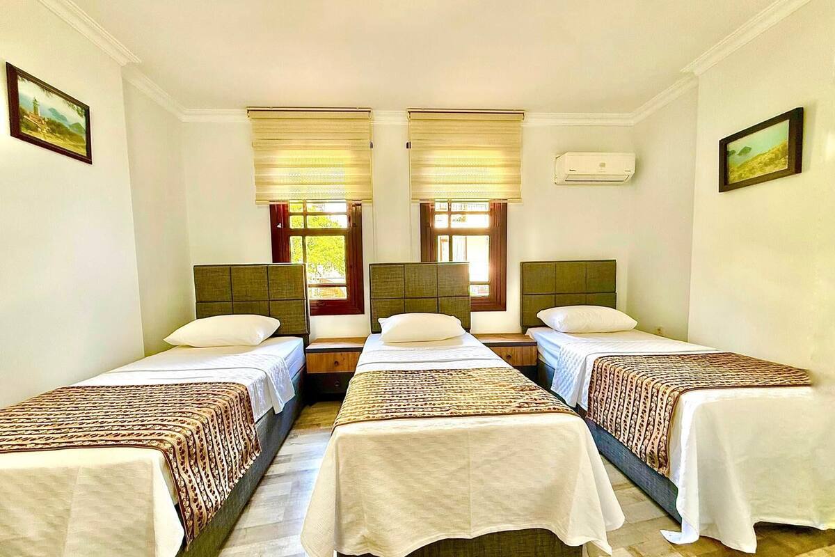Quarto de hotel com três camas de solteiro, piso de madeira e janela com persianas.