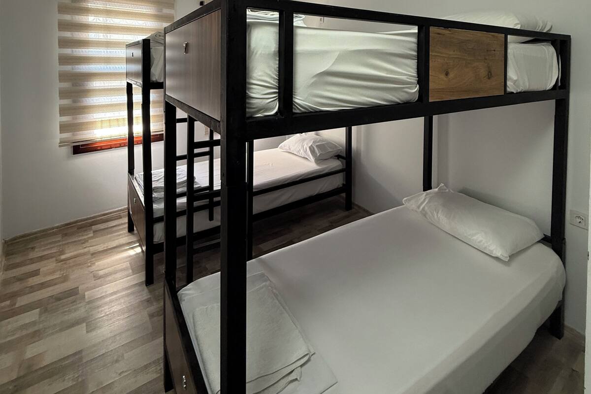 Quarto com beliche, cabeceira de madeira, janela com persianas e piso de madeira.
