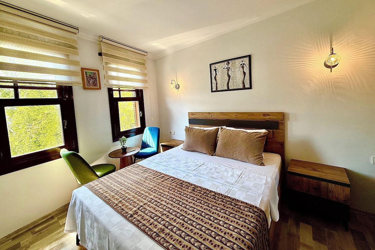 Um quarto com cama, cadeira, escrivaninha e mesa de cabeceira.