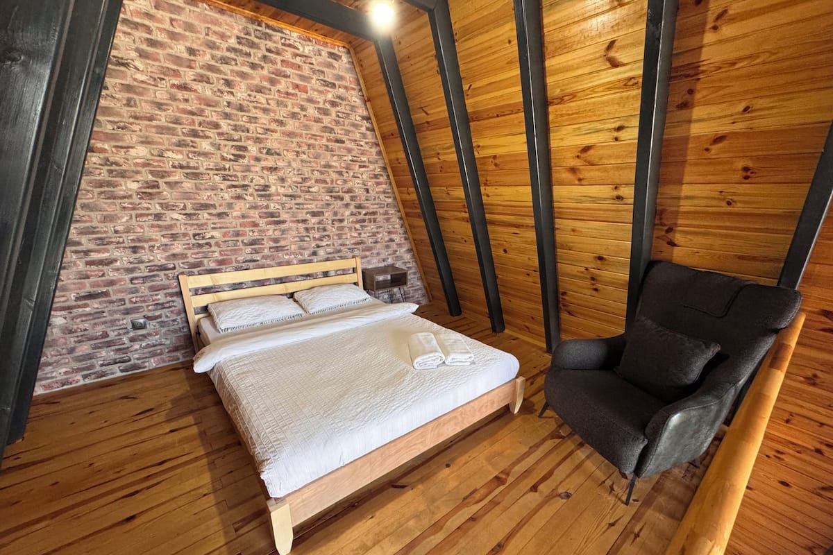 Quarto com cama de madeira, parede de tijolo e teto de madeira.