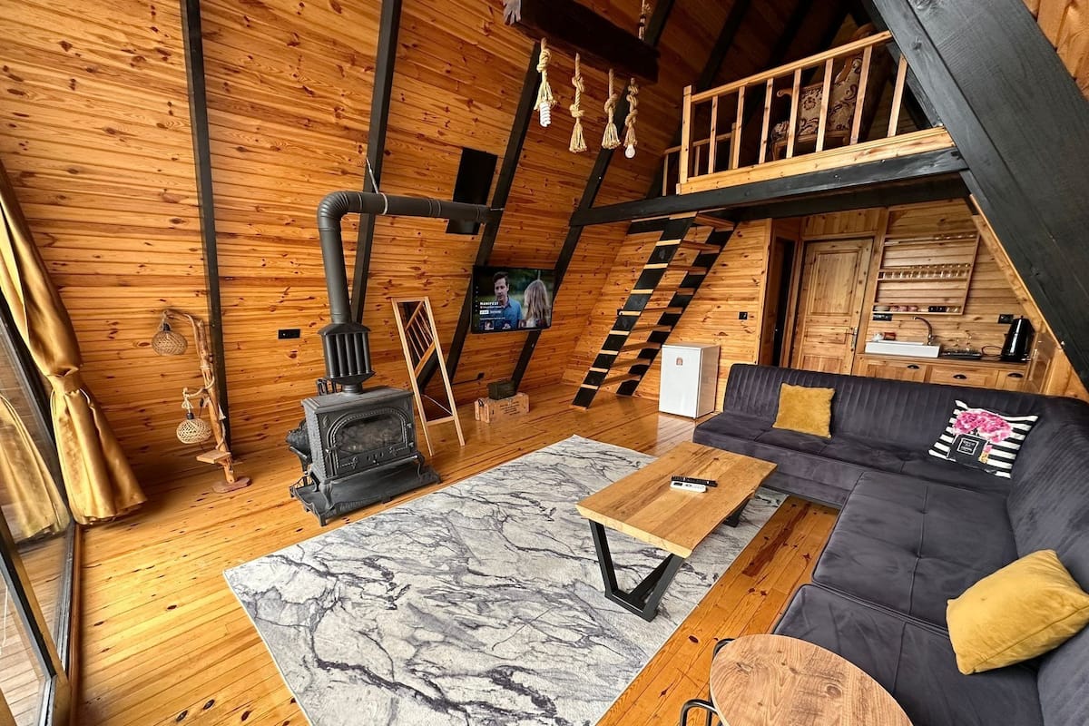 Interior acolhedor de uma cabana, com decoração em madeira, lareira, sofá e mesa de jantar.