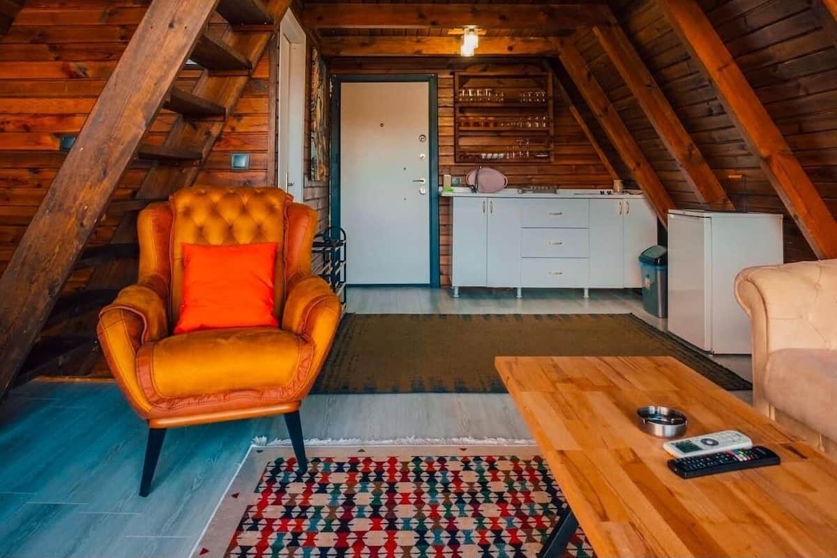 Quarto de sótão com teto de madeira, uma poltrona de couro estofada, uma mesa de centro de madeira e um tapete estampado.