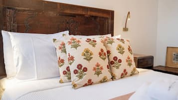 Cama com roupa de cama branca e duas almofadas decorativas com estampas florais.