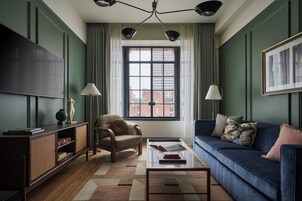 Uma sala de estar com sofá, poltrona, mesa de centro e televisão na parede.
