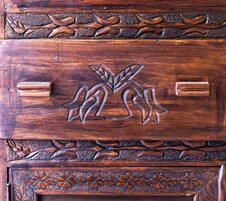 Um armário de madeira com detalhes entalhados e duas puxas metálicas.