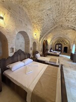 Quarto de hotel com paredes de pedra, tetos em arco e uma cama grande com cabeceira de madeira.