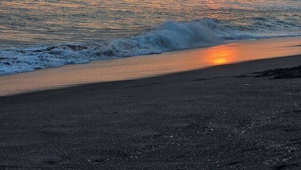 Uma praia com o sol se pondo sobre o oceano.
