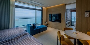 Quarto de hotel moderno com uma janela ampla, cama, sofá, área de refeições e televisão.