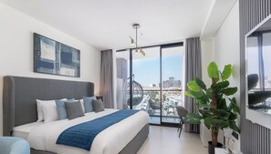 Quarto de hotel moderno com uma cama grande, vista para a cidade, uma cadeira suspensa e um vaso com planta.