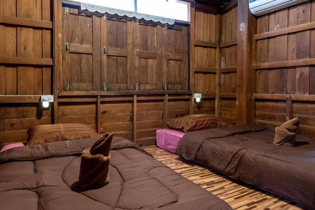 Quarto de madeira com beliches, lambris e janela com cortina de renda.