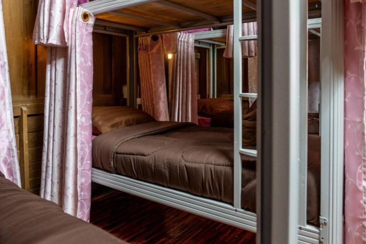 Uma cama de beliche com cabeceira de madeira, uma mesinha de cabeceira e uma cortina rosa.