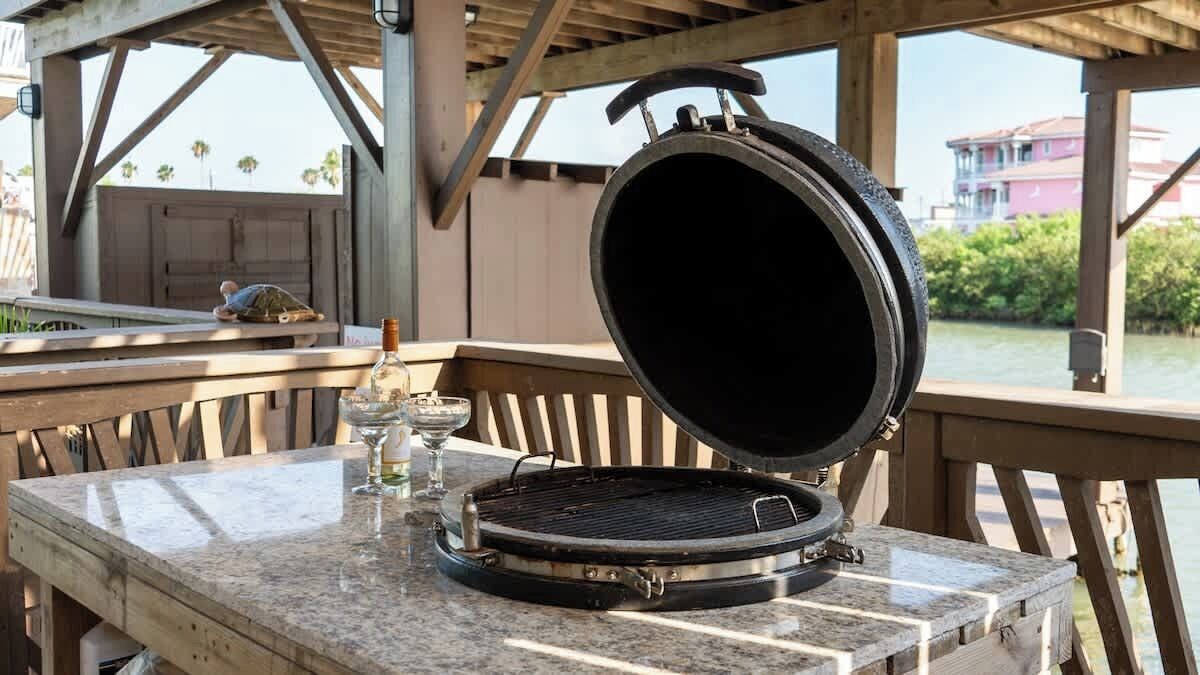 Um churrasco portátil sobre uma mesa de madeira, com uma taça de vinho e uma garrafa.