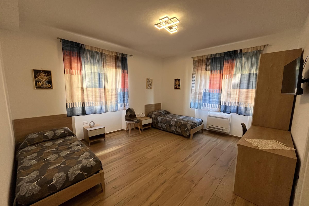 Quarto com duas camas, uma mesinha, uma cadeira, aquecedor e televisão.