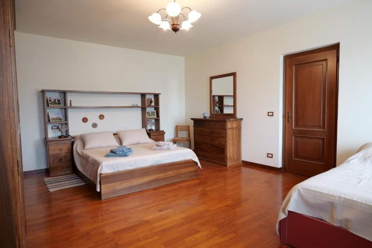 Quarto com cama de madeira, cômoda, espelho e prateleira com fotos.