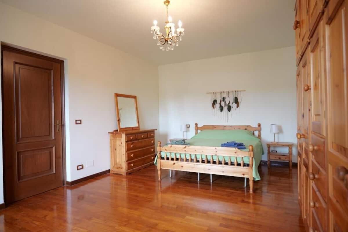 Quarto com cama de madeira, penteadeira, espelho e lustre.