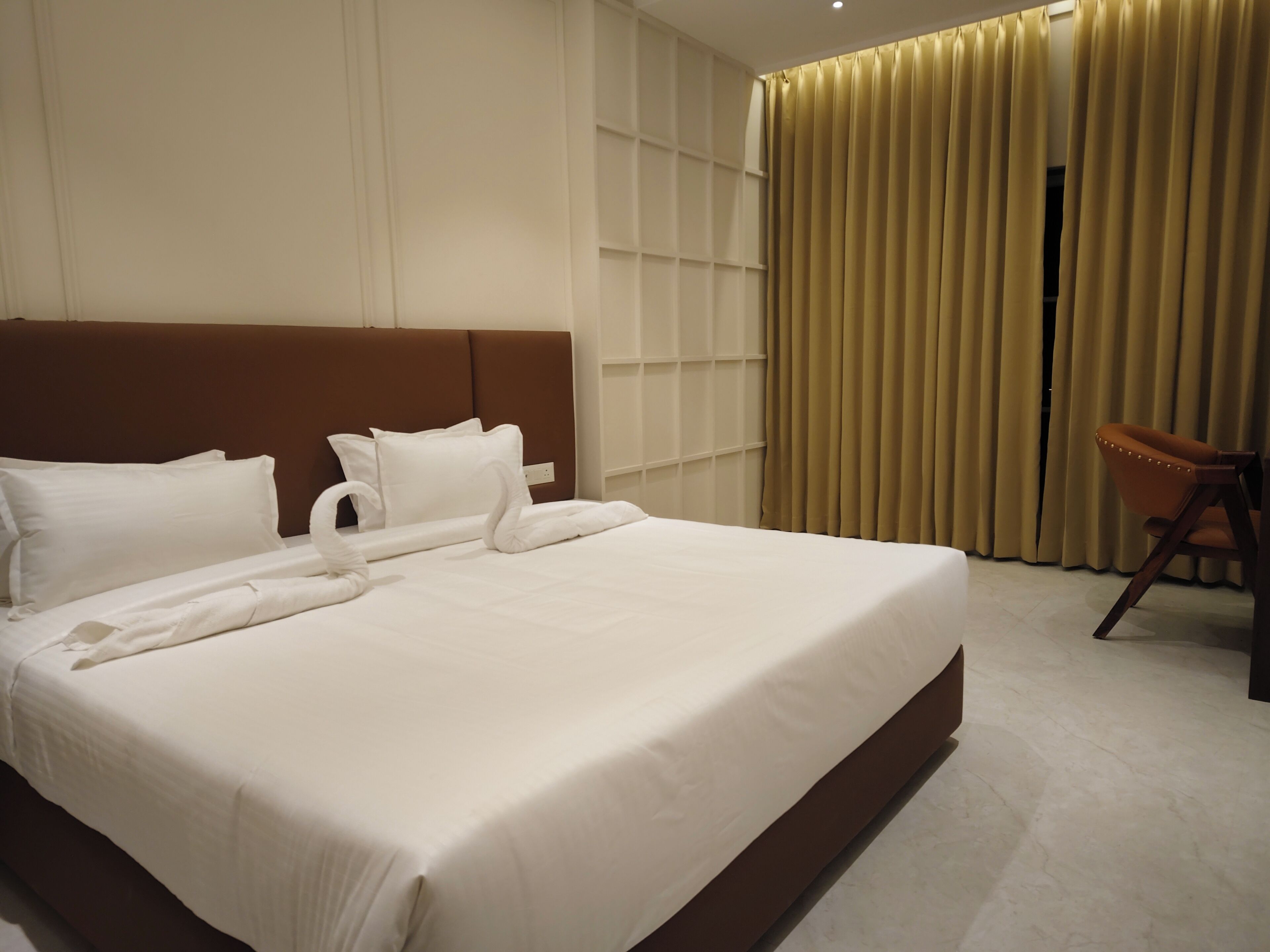 Quarto de hotel com uma cama grande, cabeceira, uma cadeira e cortina.
