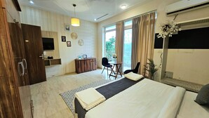 Quarto de hotel com cama, escrivaninha, cadeira, televisão e janela com cortinas.