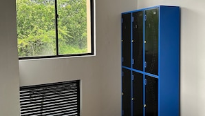 Quarto com uma janela grande, um móvel de armazenamento azul, um radiador e uma mesa com cadeiras.