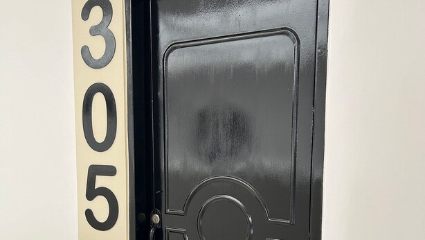 Uma porta preta com puxador circular e o número '305' na parede ao lado.