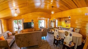 Interior em madeira com sofá, televisão, mesa de jantar e cozinha.