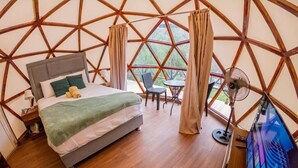 Um quarto com cama, escrivaninha, cadeira, ventilador e uma janela grande.