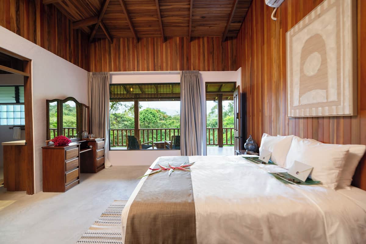 Quarto com uma cama grande, paredes de madeira, cômoda e vista para o exterior.