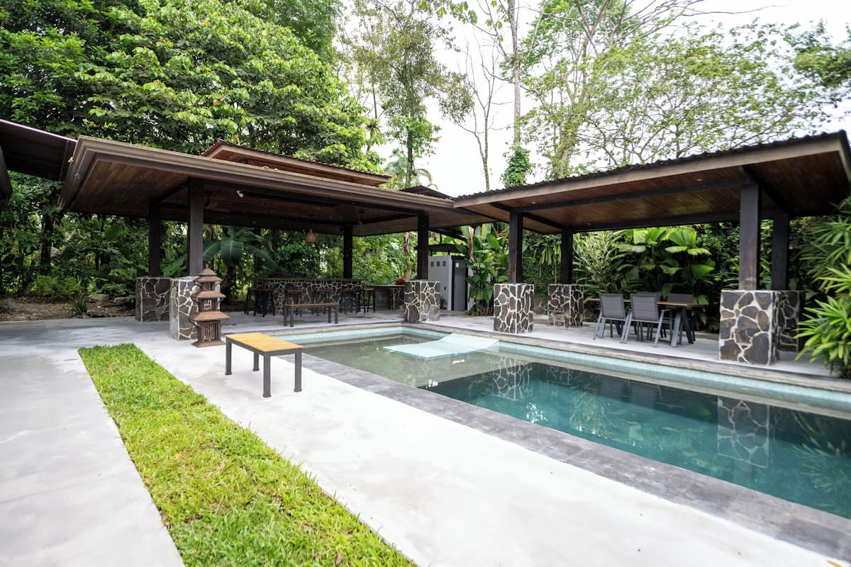 Uma área de piscina com terraço coberto, paredes de pedra e mobiliário para exterior.
