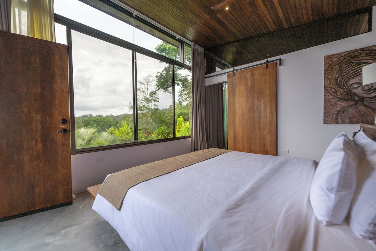 Quarto com uma janela grande, uma cama e teto de madeira.