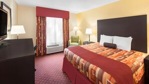 Quarto de hotel com cama, escrivaninha, cadeira, televisão e janela com cortinas.