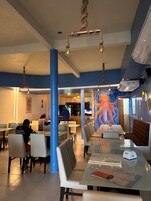 Interior de restaurante com mesas, cadeiras, área de bar e um grande mural de polvo na parede.