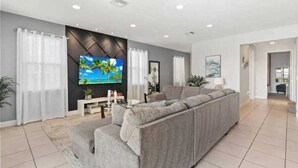 Uma sala de estar moderna com um amplo sofá modular cinza, uma TV de tela plana e um painel decorativo na parede.